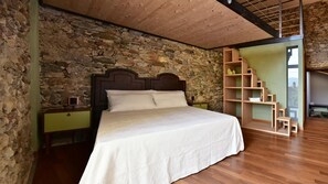 Quarto com parede de pedra, teto de madeira e cama com cabeceira de madeira.