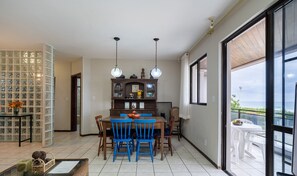 Uma sala de jantar com mesa de madeira e cadeiras azuis, uma mesa de centro de vidro e um armário com portas de vidro.