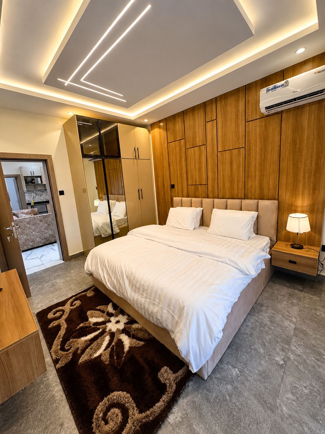 Quarto moderno com cama grande, parede de painéis de madeira, armário embutido e ar condicionado.