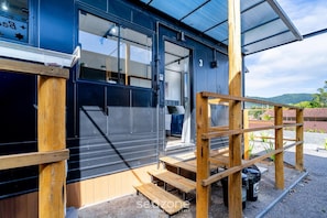 Um edifício moderno com fachada preta, escadas de madeira que levam a uma porta e uma área externa coberta.