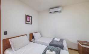 Quarto de hotel com duas camas, ar condicionado fixado na parede e um quadro emoldurado.