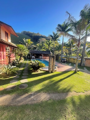 Área residencial com piscina, palmeiras e uma casa de fachada vermelha.