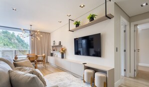 Uma sala de estar moderna com sofá, TV e área de jantar com mesa e cadeiras.