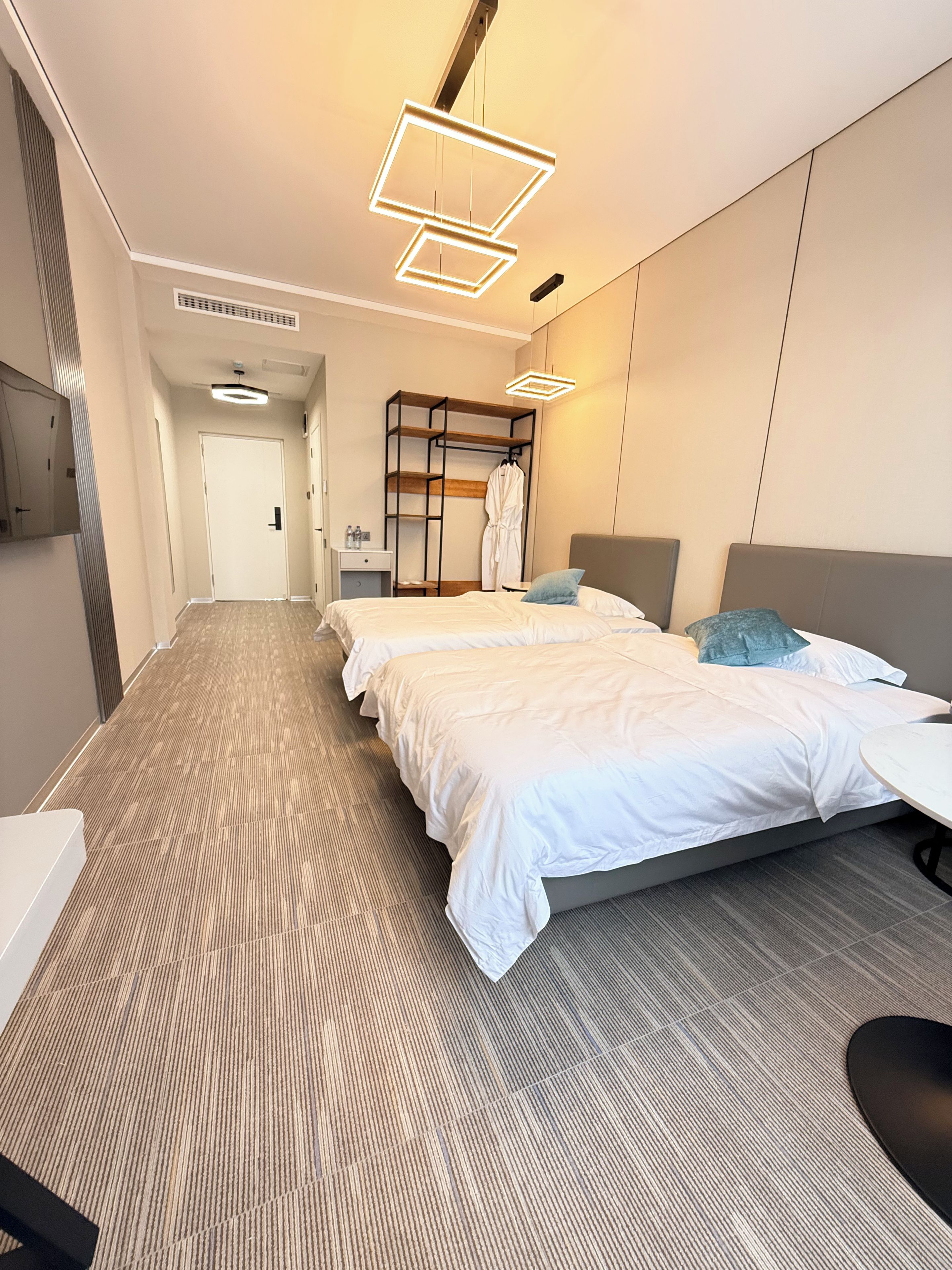Quarto de hotel com duas camas, um guarda-roupa, uma escrivaninha e um banheiro.