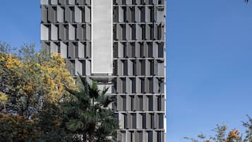 Um edifício moderno com fachada em forma de grade, cercado por vegetação e árvores.