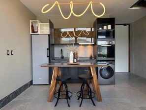 Uma cozinha moderna com ilha central, banquetas, máquina de lavar e forno embutido.