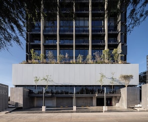 Um edifício moderno de vários andares com terraço plano, grandes janelas e base de concreto.