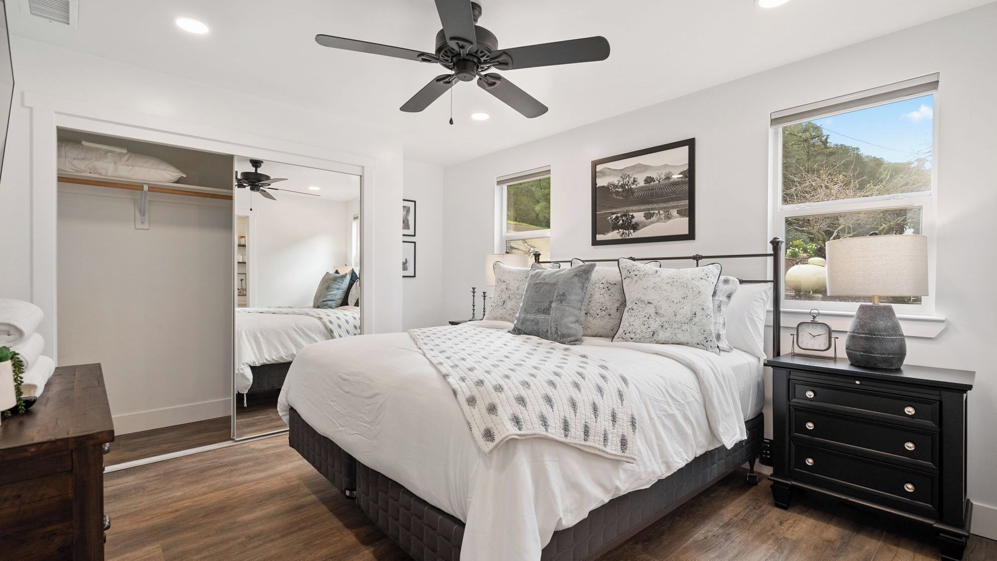 Um quarto com cama, mesas de cabeceira, ventilador de teto, janela com vista e cômoda.