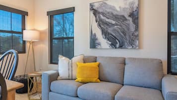 Uma sala de estar com um sofá cinzento, um travesseiro amarelo e um grande quadro abstrato na parede.