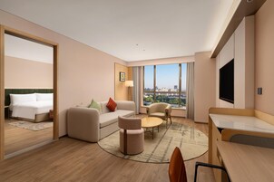 Quarto de hotel moderno com cama, sofá, poltrona e televisão.