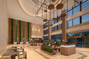 Um hall espaçoso com balcão de recepção, área de estar e grandes janelas com vista para a paisagem urbana.