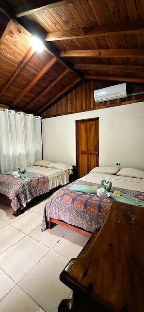 Quarto com duas camas, teto de madeira, uma porta e ar condicionado.