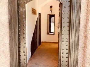 Corredor com porta de metal e janela, dando acesso a um quarto com piso ladrilhado.