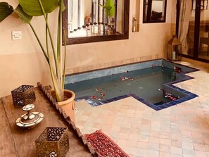 Pequena piscina coberta com chão de azulejos, rodeada por objetos decorativos e plantas.