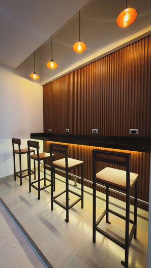 Uma área de bar com painéis de madeira, três banquetas e iluminação pendente.