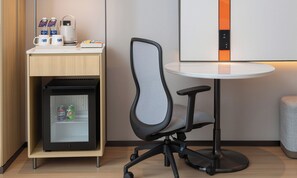 Um espaço de trabalho compacto com uma cadeira moderna, uma pequena geladeira e uma mesa com luminária.