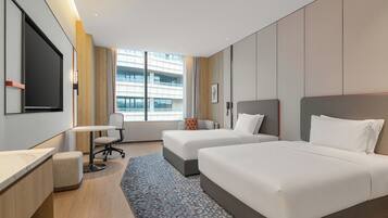 Quarto de hotel com duas camas, uma mesa de escritório, uma cadeira, uma janela grande e vista para um edifício.