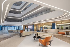 Um hall amplo com área de estar central, balcão de recepção e escadaria moderna.