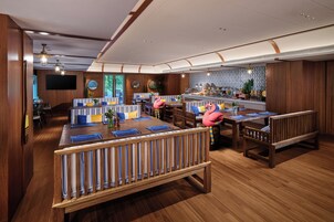 Um restaurante com mobiliário de madeira, almofadas listradas e um balcão central.