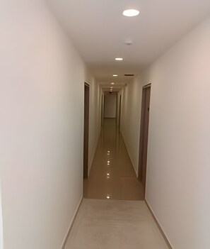 Um corredor estreito e bem iluminado com piso refletivo, que leva a uma porta no final.