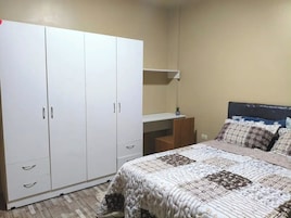 Quarto com cama, guarda-roupa e mesa de cabeceira.