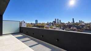 Terraço no telhado com vista para o horizonte da cidade, céu limpo e sol brilhando.