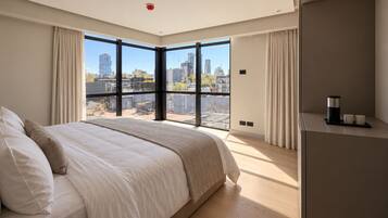 Quarto moderno com cama grande, vista panorâmica da cidade através de janelas do chão ao teto e decoração minimalista.