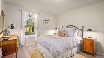 Quarto com cama, duas mesas de cabeceira, escrivaninha, cadeira, janela com cortinas e quadro na parede.