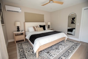 Quarto com cama, mesas de cabeceira, ventoinha no teto, ar condicionado, tapete estampado e espelho.