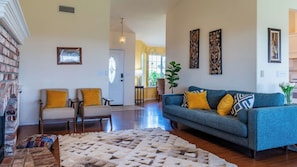 Uma sala de estar com um sofá azul, duas poltronas, um tapete estampado e uma parede de tijolos.