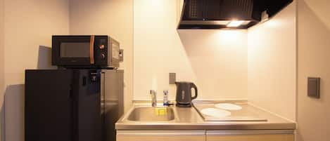 Uma cozinha compacta com micro-ondas sobre a geladeira, chaleira no balcão e pia com torneira.