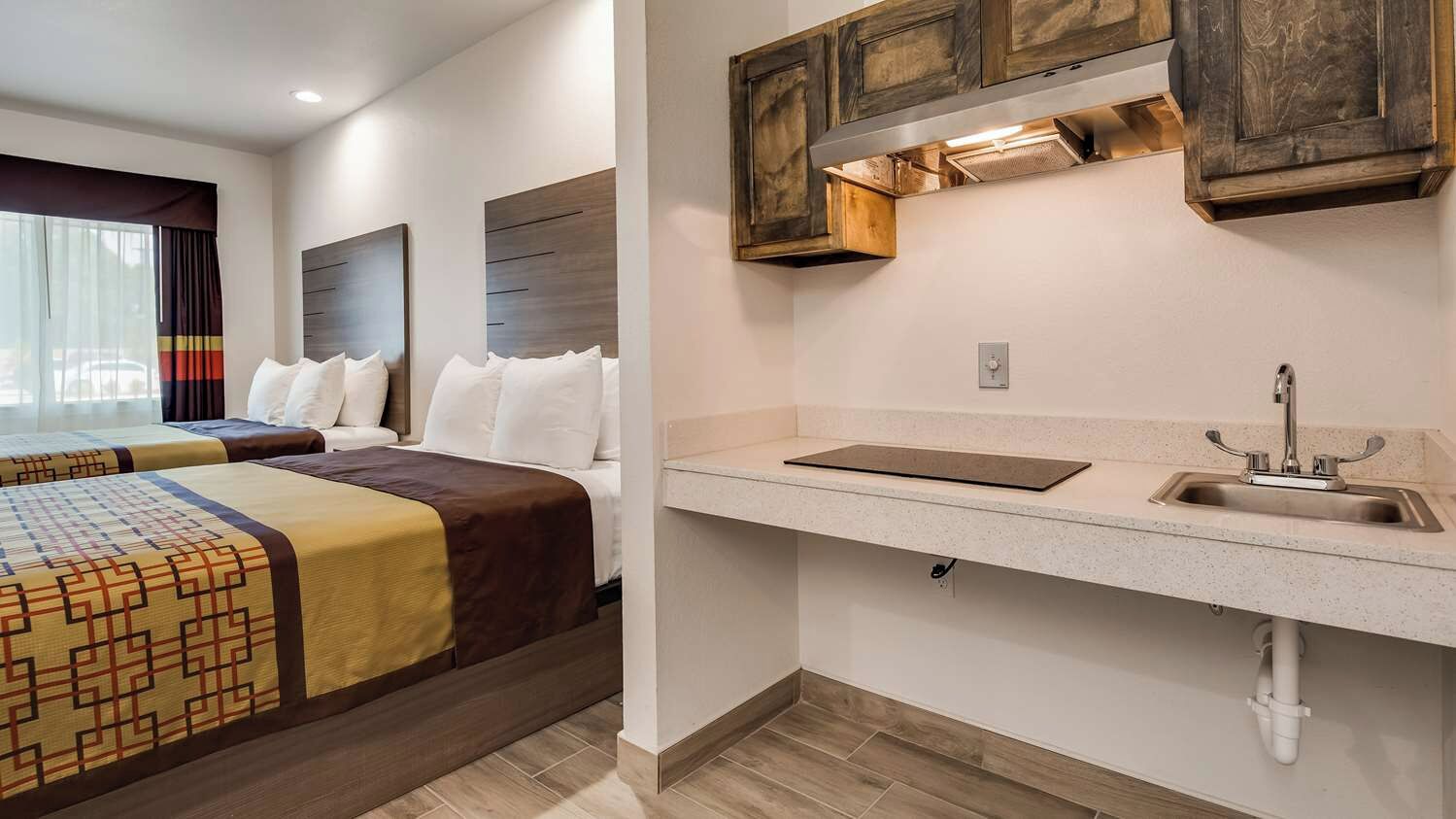 Quarto de hotel com cama, mesa de cabeceira, prateleira embutida e janela com cortinas.