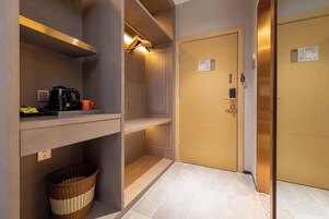 Um corredor com porta de madeira, luminária na parede, cesta e máquina de café em uma prateleira.