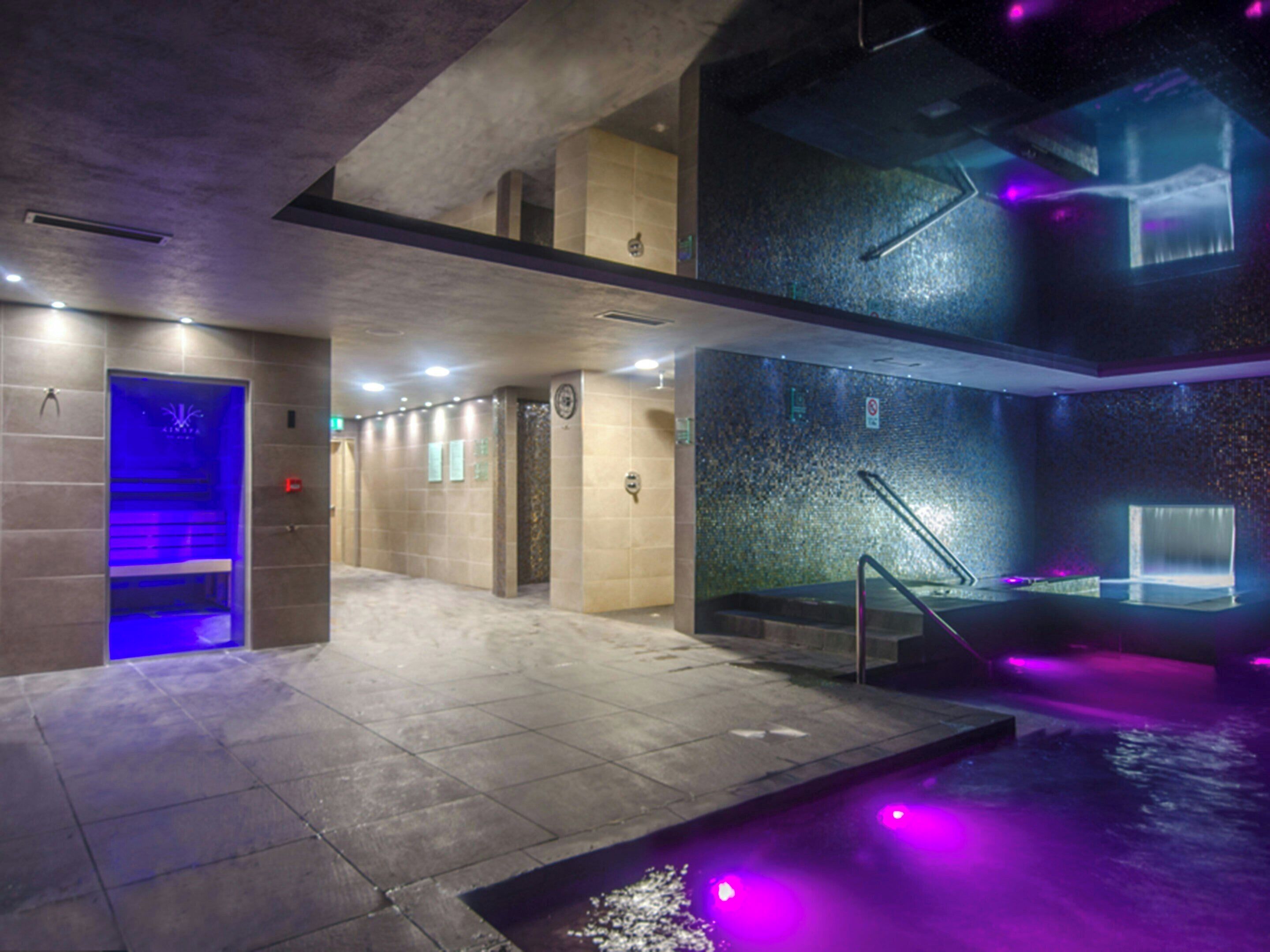 Uma área interna moderna com piscina, uma banheira de hidromassagem envidraçada, uma escadaria e uma área de recepção.