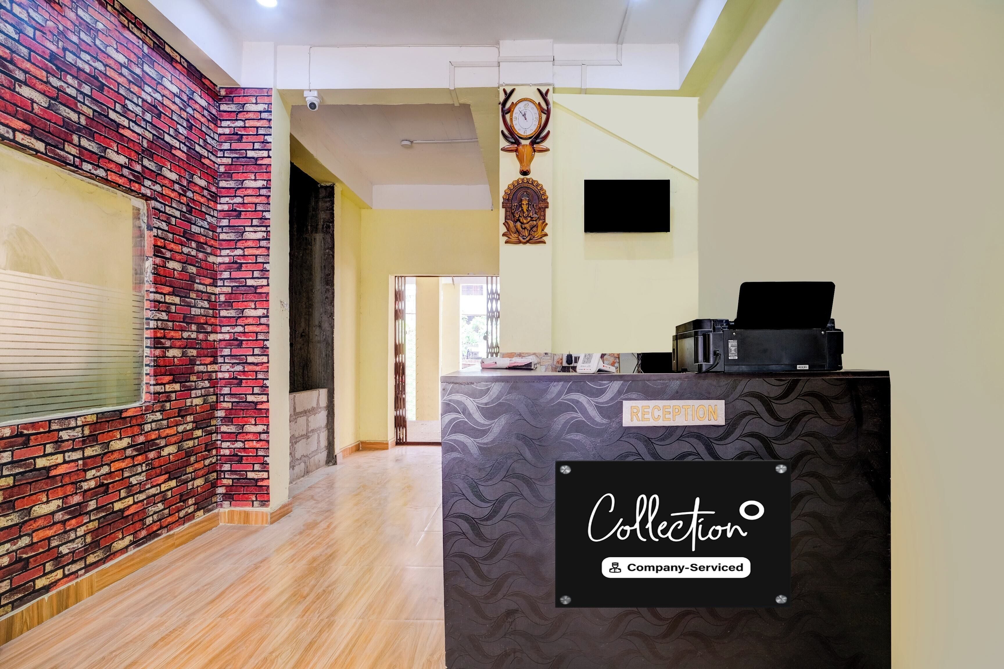 Uma área de recepção com balcão identificado como 'Reception' e 'Company Serviced', uma parede decorativa com padrão de tijolos e uma câmera de segurança instalada no teto.