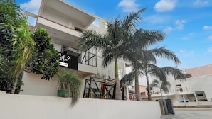 Um edifício moderno com varanda, rodeado por vegetação e palmeiras.