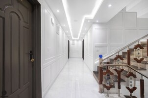 Um corredor com escada, paredes brancas e uma porta à esquerda.