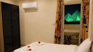 Quarto de hotel com duas camas, um guarda-roupa, um aparelho de ar condicionado e vista para as pirâmides à noite.