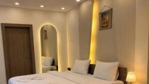 Quarto de hotel moderno com uma cama grande, uma mesa de cabeceira com abajur, um espelho fixado na parede e uma banheira de hidromassagem.
