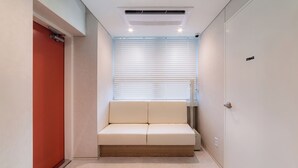 Um quarto pequeno com sofá, uma porta e janela com persianas.