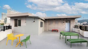 Terraço no terraço com área de estar, cadeiras verdes e amarelas, um pequeno banco vermelho e vista para o horizonte da cidade.