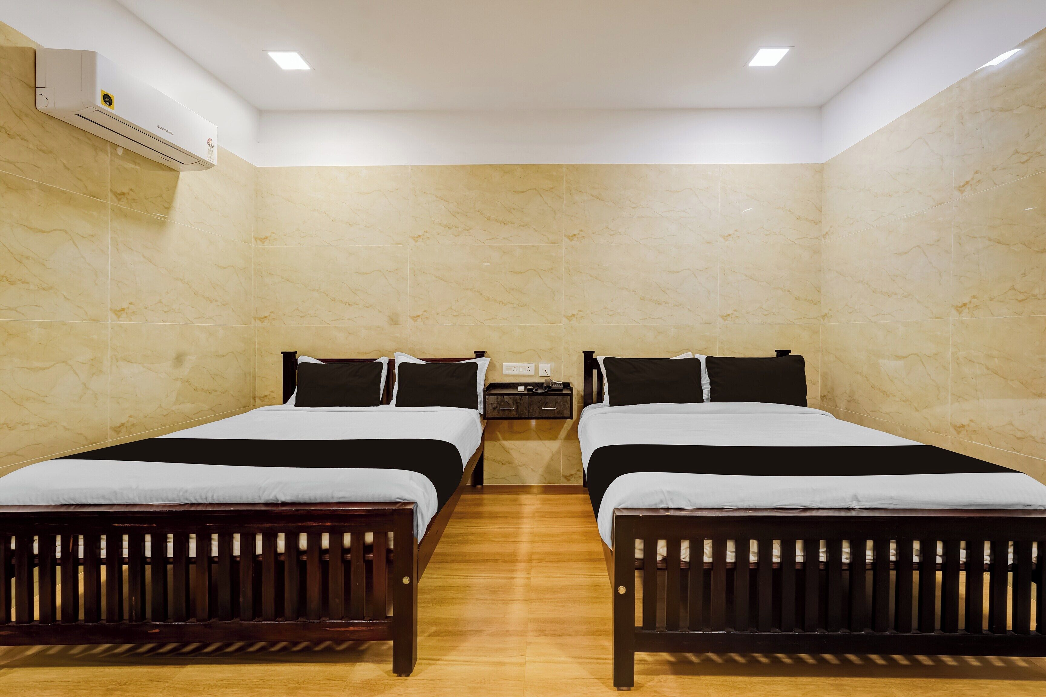 Quarto de hotel com duas camas, uma mesa de cabeceira e um ar condicionado fixado na parede.