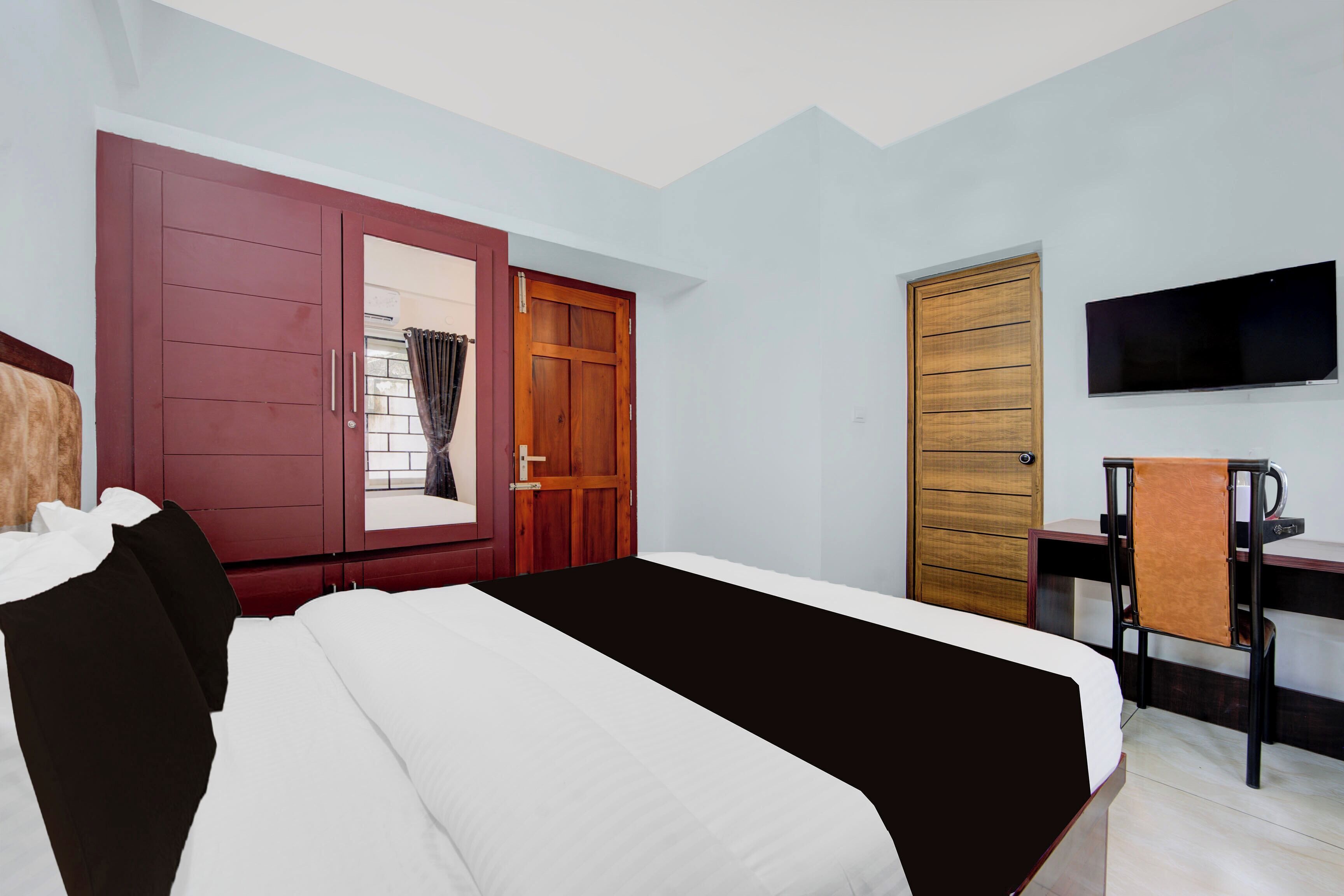 Quarto de hotel com cama, secretária, cadeira, televisão e duas portas.