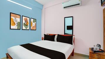 Quarto de hotel com cama, mesa de cabeceira com abajur, ar condicionado e três quadros na parede.