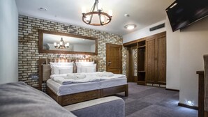 Quarto com parede de tijolos, uma cama grande, guarda-roupa de madeira e televisão de tela plana fixada na parede.