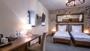 Quarto de hotel com escrivaninha, duas camas, parede de tijolos e um candelabro.