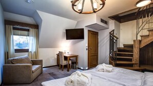 Quarto de hotel com cama, escrivaninha, cadeira, televisão e escada.