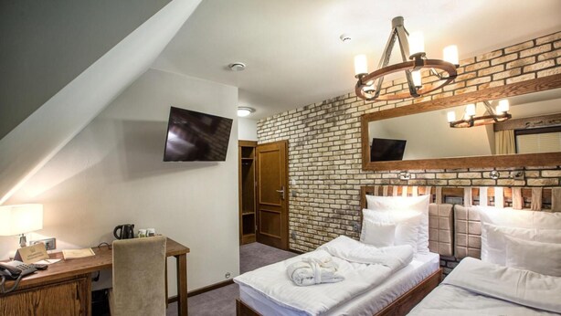 Quarto de hotel com cama, escrivaninha, cadeira, televisão e parede de tijolos.