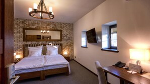 Quarto de hotel com parede de tijolos, cama com roupa branca, escrivaninha com cadeira, TV de tela plana e lustre.