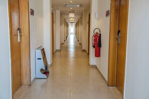 Corredor de hotel com portas em ambos os lados, um extintor de incêndio fixado na parede da direita e uma lousa branca apoiada na parede da esquerda.